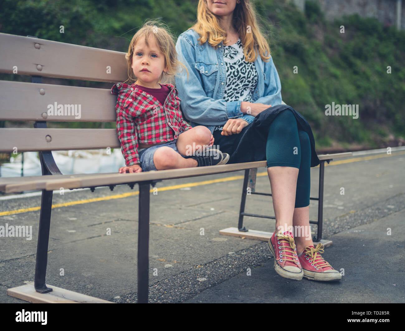 A young mother and her toddler are sitting on a bench at the strain ...