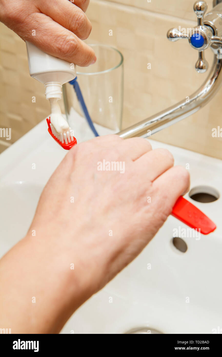 Red toothbrush and tube of toothpaste in female hands with a water tap ...