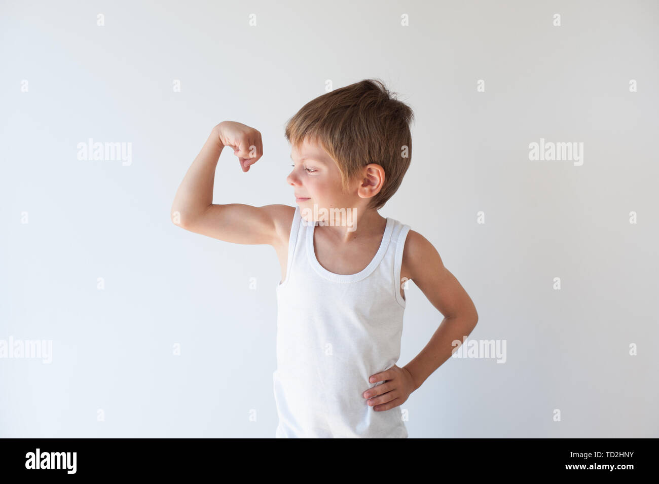 strong little boy in white tank top showing muscles with smile on his ...