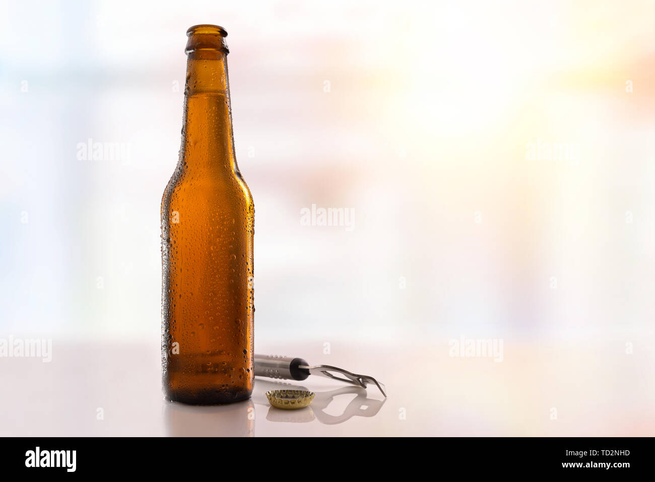 Beer bottle filled and open on glass table with bottle opener and light ...