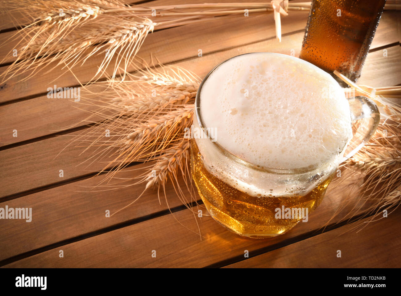 Pitcher full of beer with foam and bottle behind on wooden table ...