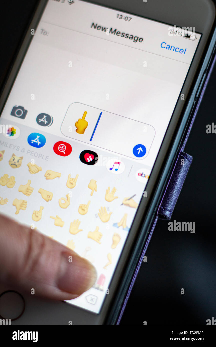 mobile phone showing someone typing the middle finger emoji, on a black ...