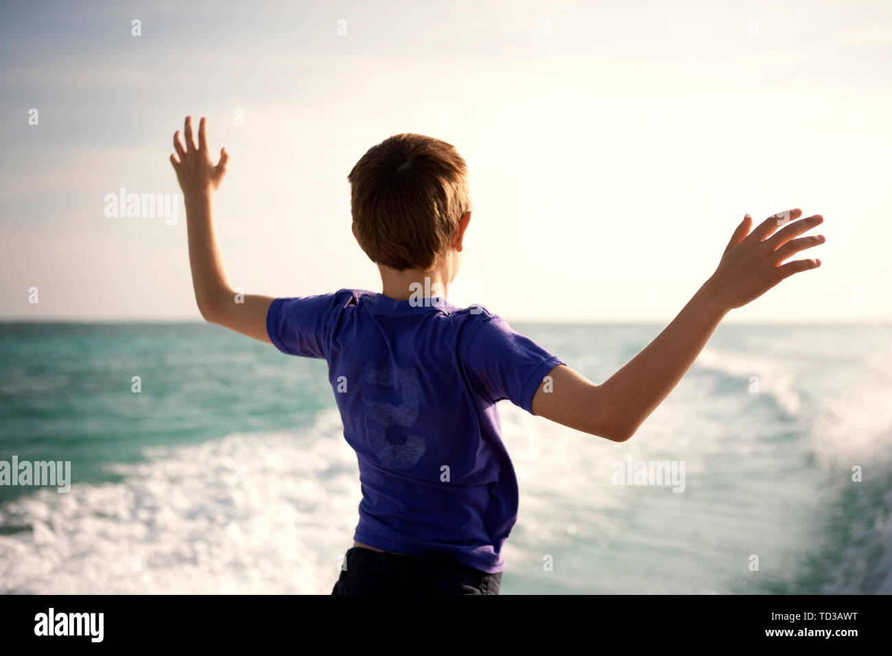 Boy standing with his arms raised while watching waves in a rough sea ...