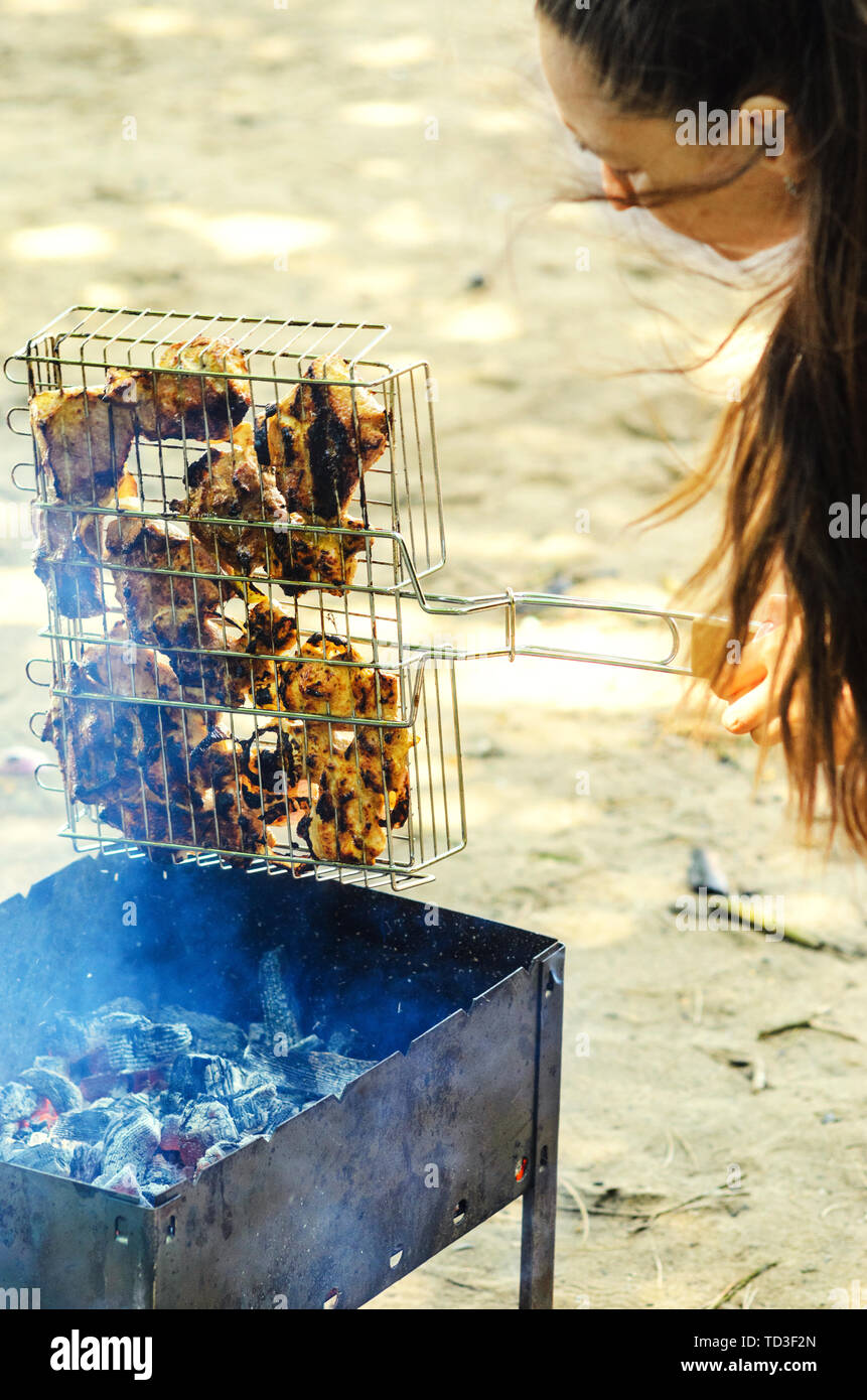 Woman with long dark hair hold a grid of grill with chicken meat over ...