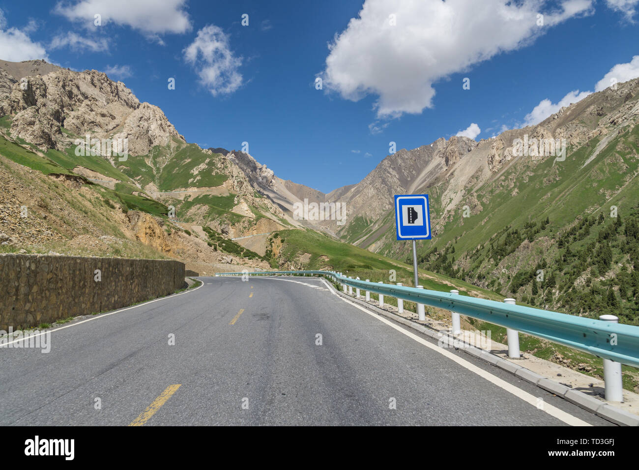 G217 Duku Highway bend in alpine forest under summer blue sky and white ...
