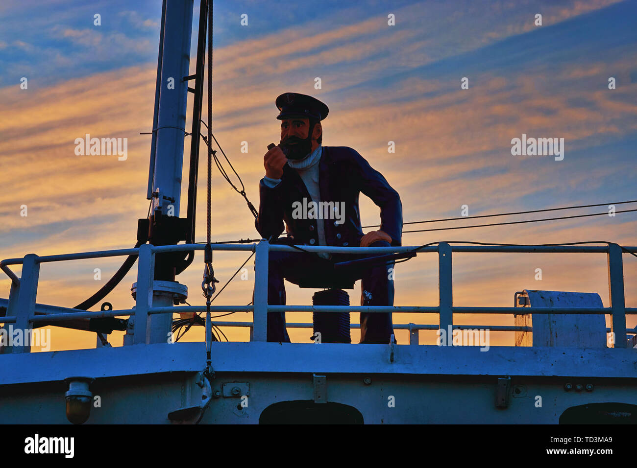 Sailor figure sits on the deck of a boat. With sunset in the background ...