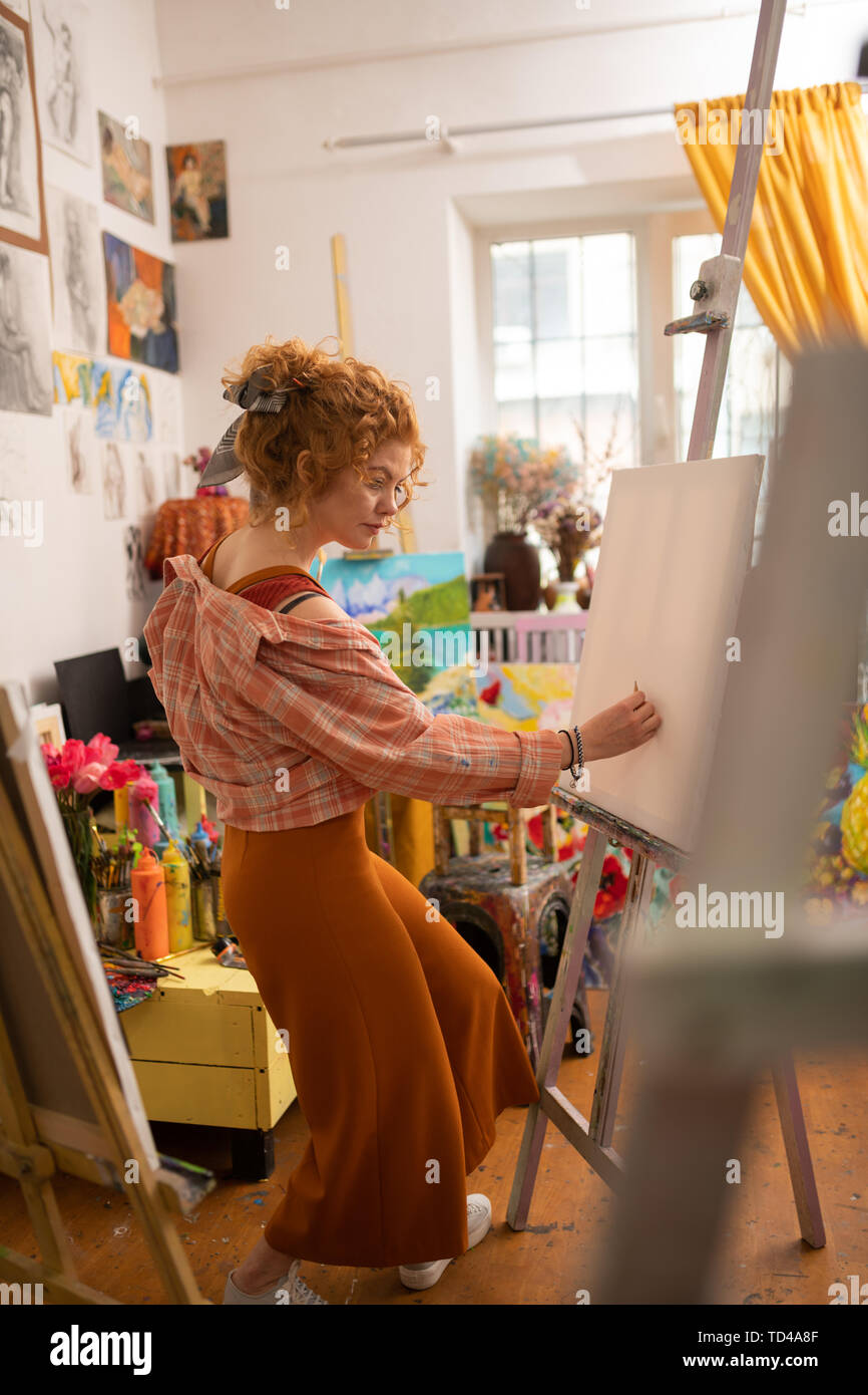 Relaxed drawing. Curly young artist with brassy hair drawing at the ...