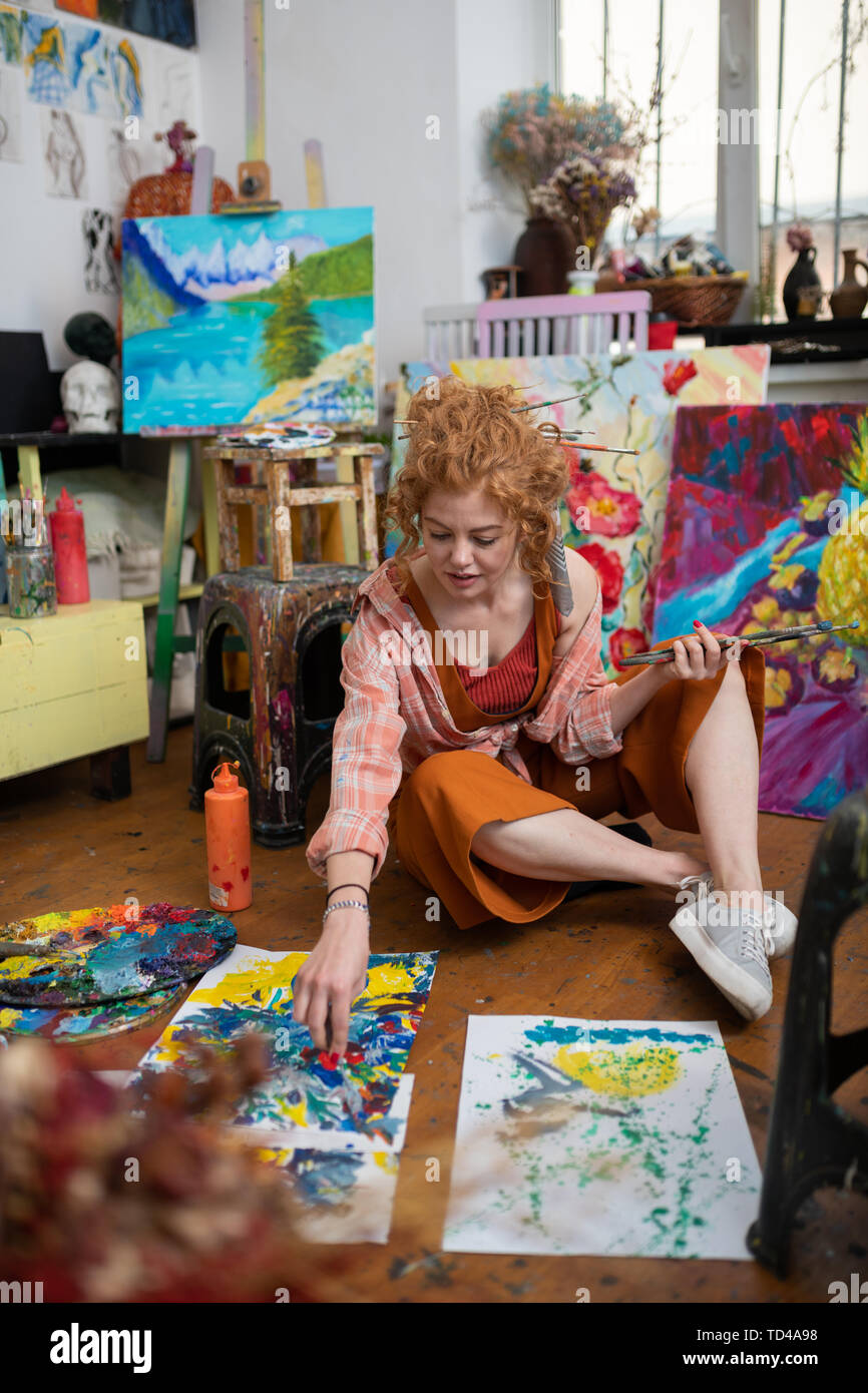 Coloring on floor. Red-haired talented creative woman wearing orange ...
