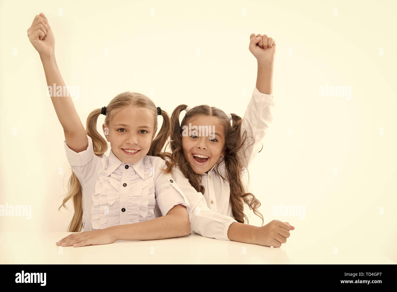 Schoolgirls happy keep hands up while sit at desk white background. Win ...