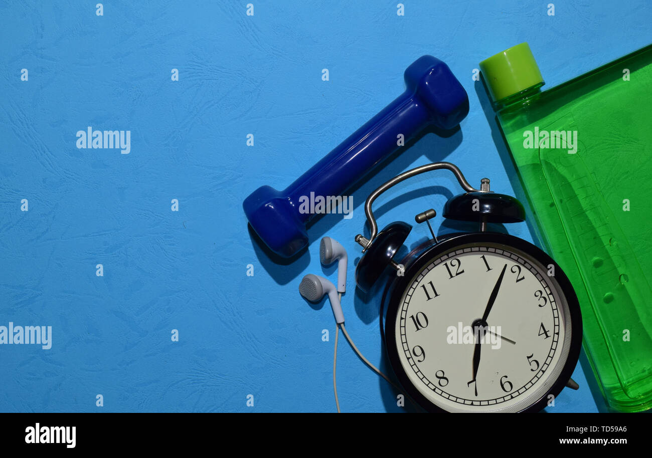 blue dumbbell, alarm clock and bottle indicating workout plan on blue ...