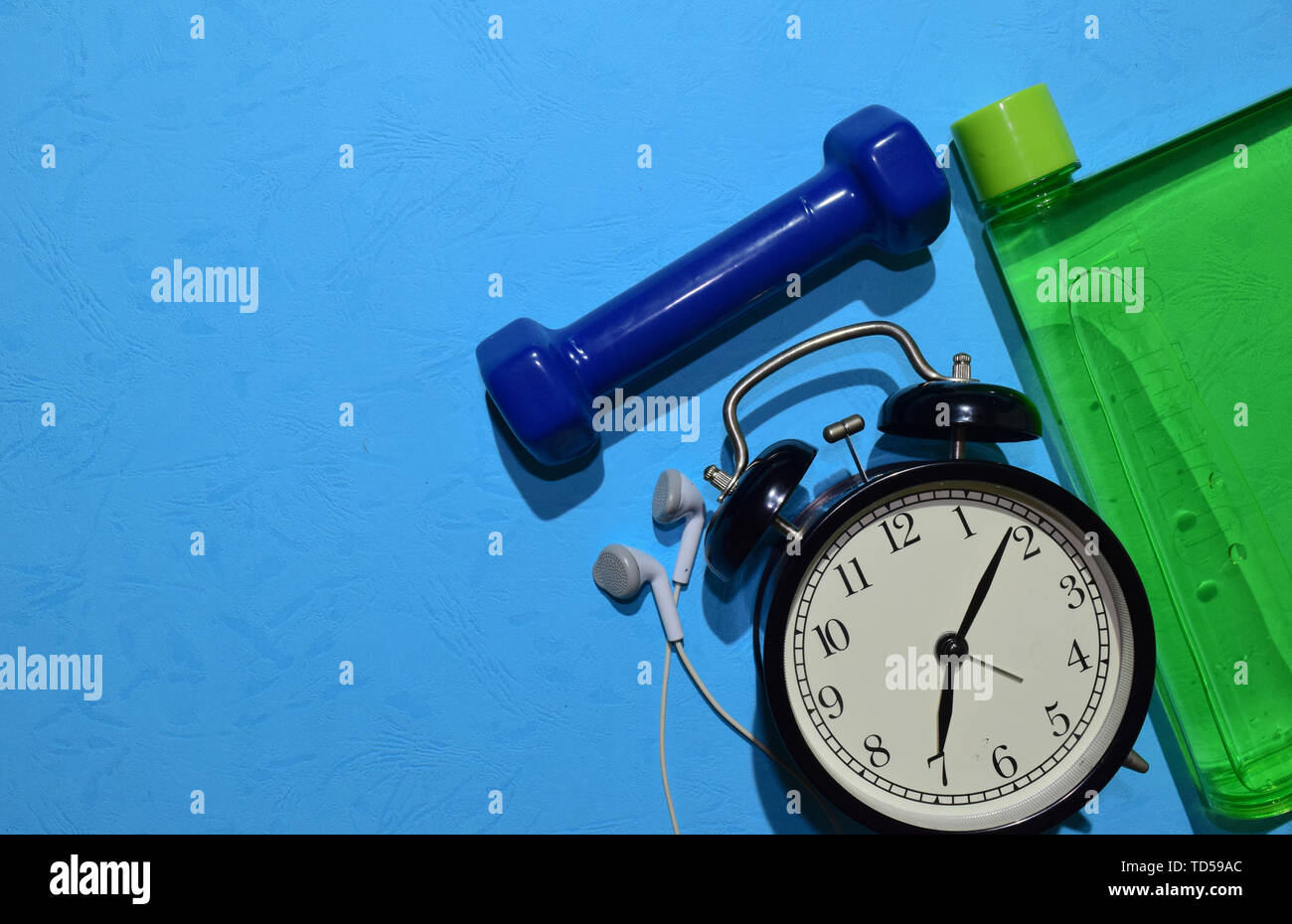 blue dumbbell, alarm clock and bottle indicating workout plan on blue ...