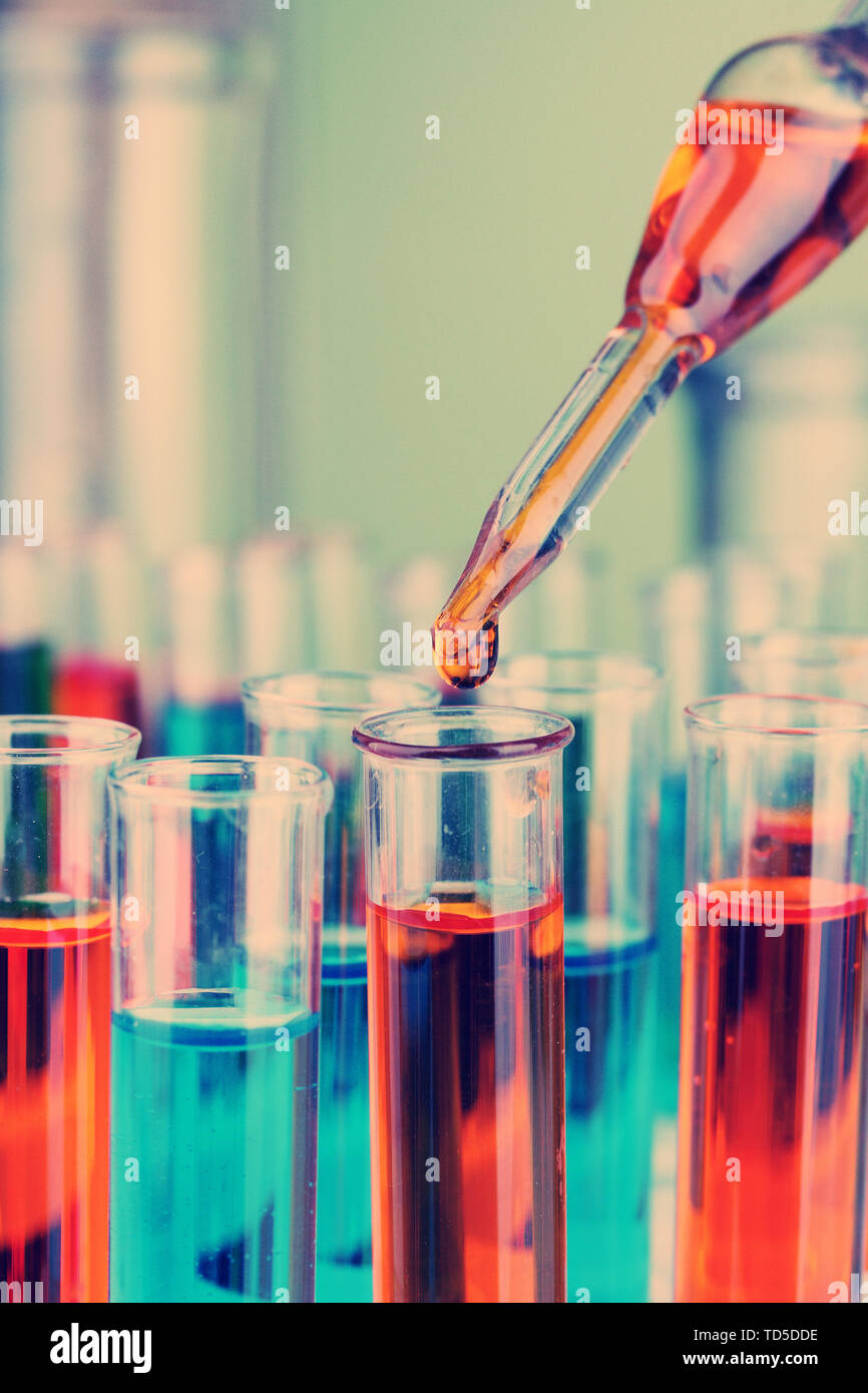 Laboratory pipette with drop of color liquid over glass test tubes ...