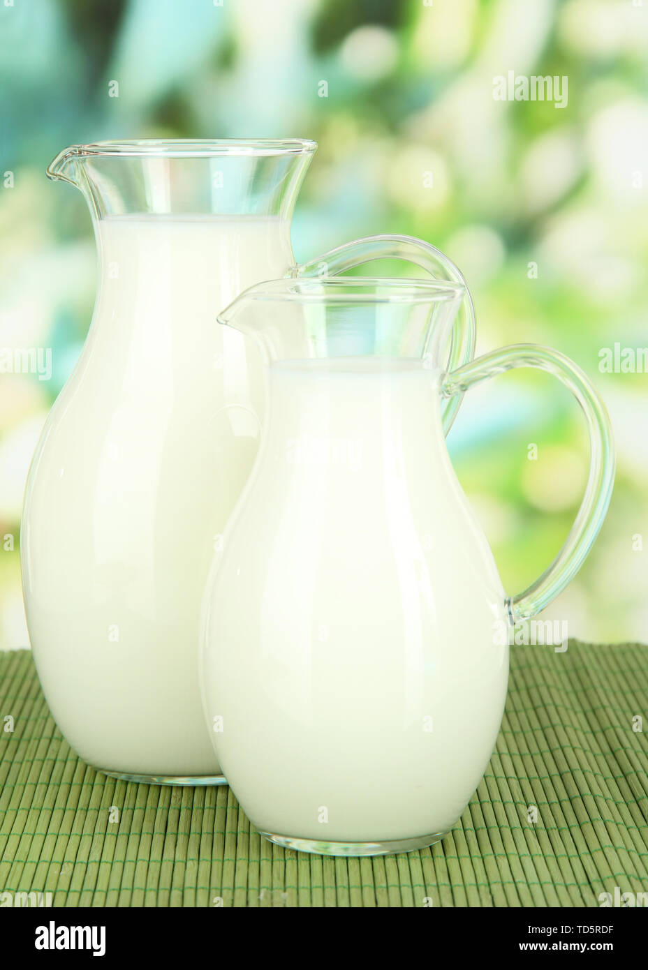 Pitchers of milk on table on bright background Stock Photo - Alamy