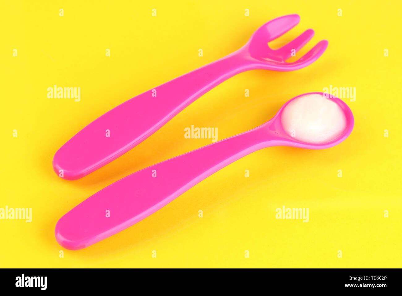 Pink spoon and fork for baby food on yellow background Stock Photo - Alamy