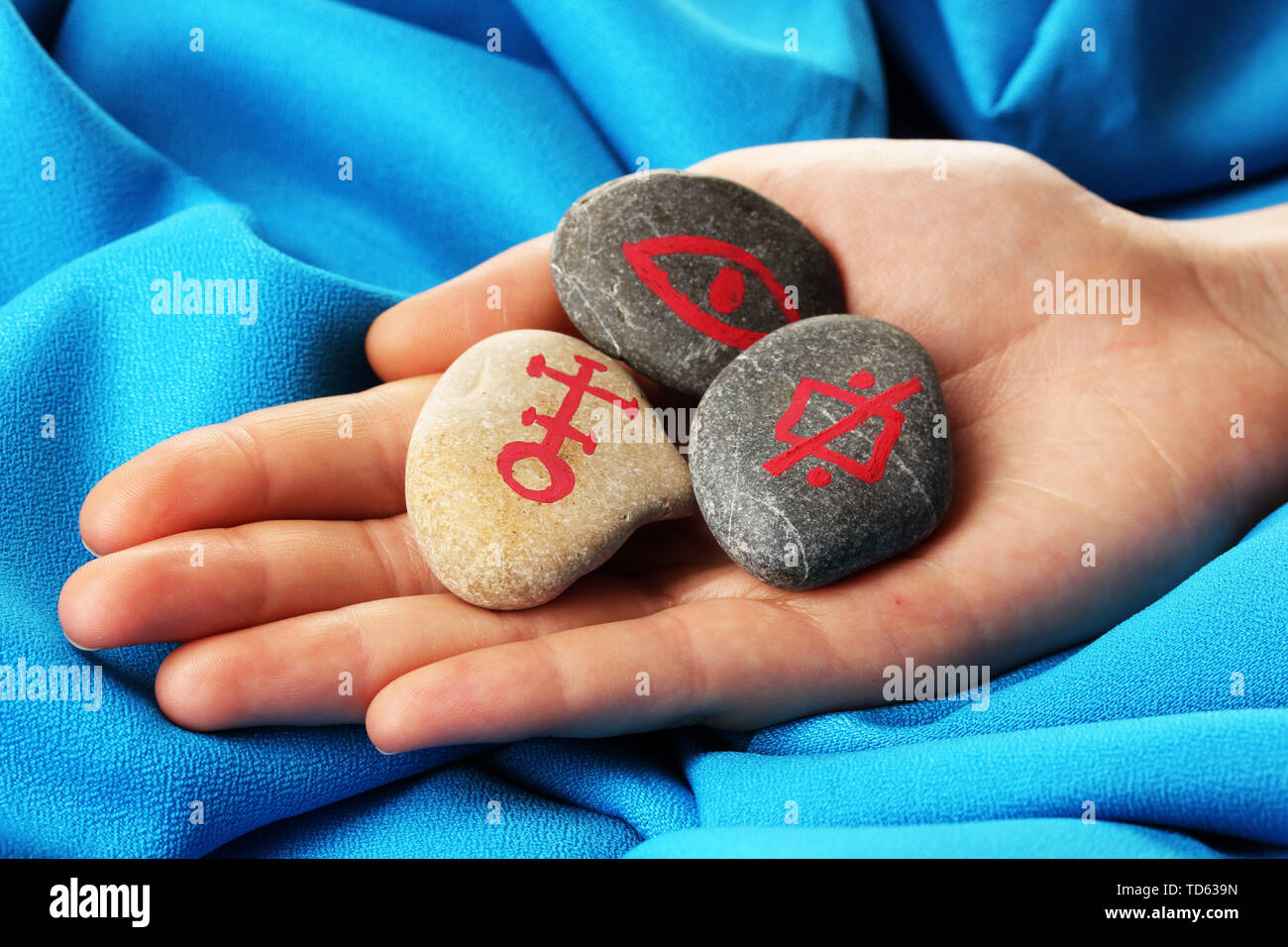 Fortune telling with symbols on stone in hand on blue fabric background ...