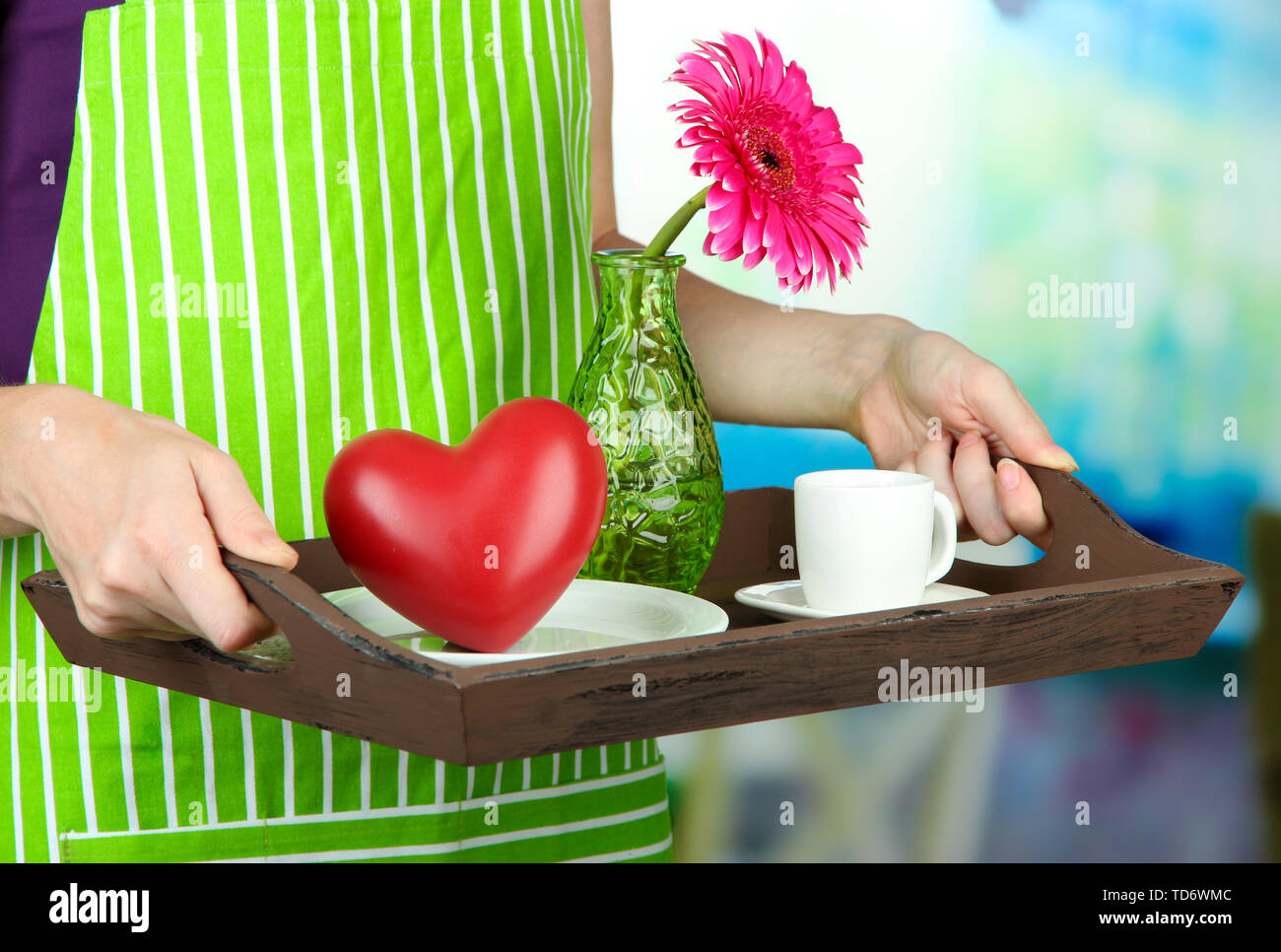 Woman in green apron holding wooden tray with breakfast, on bright ...