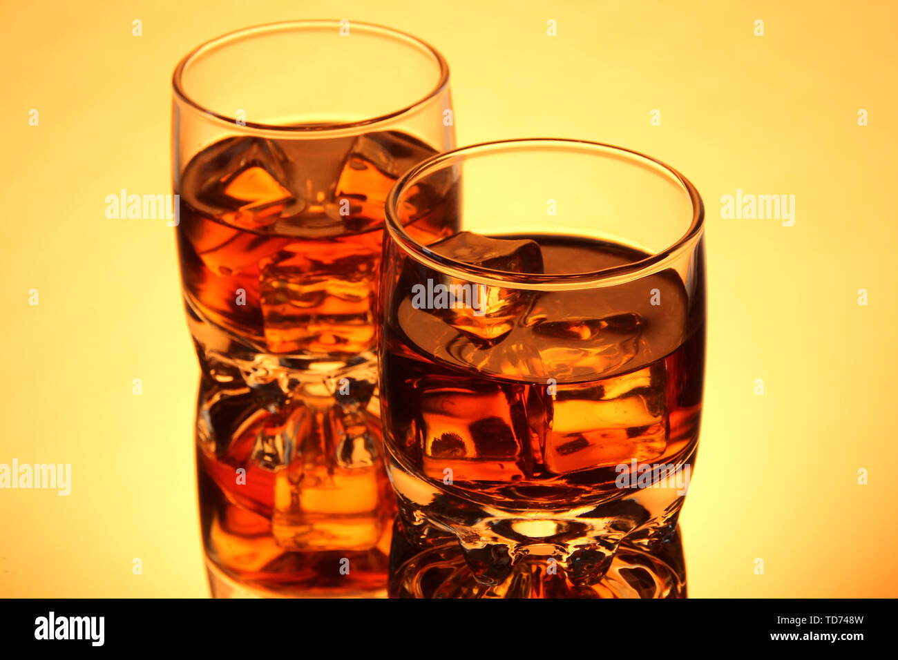 Brandy glasses with ice on yellow background Stock Photo - Alamy