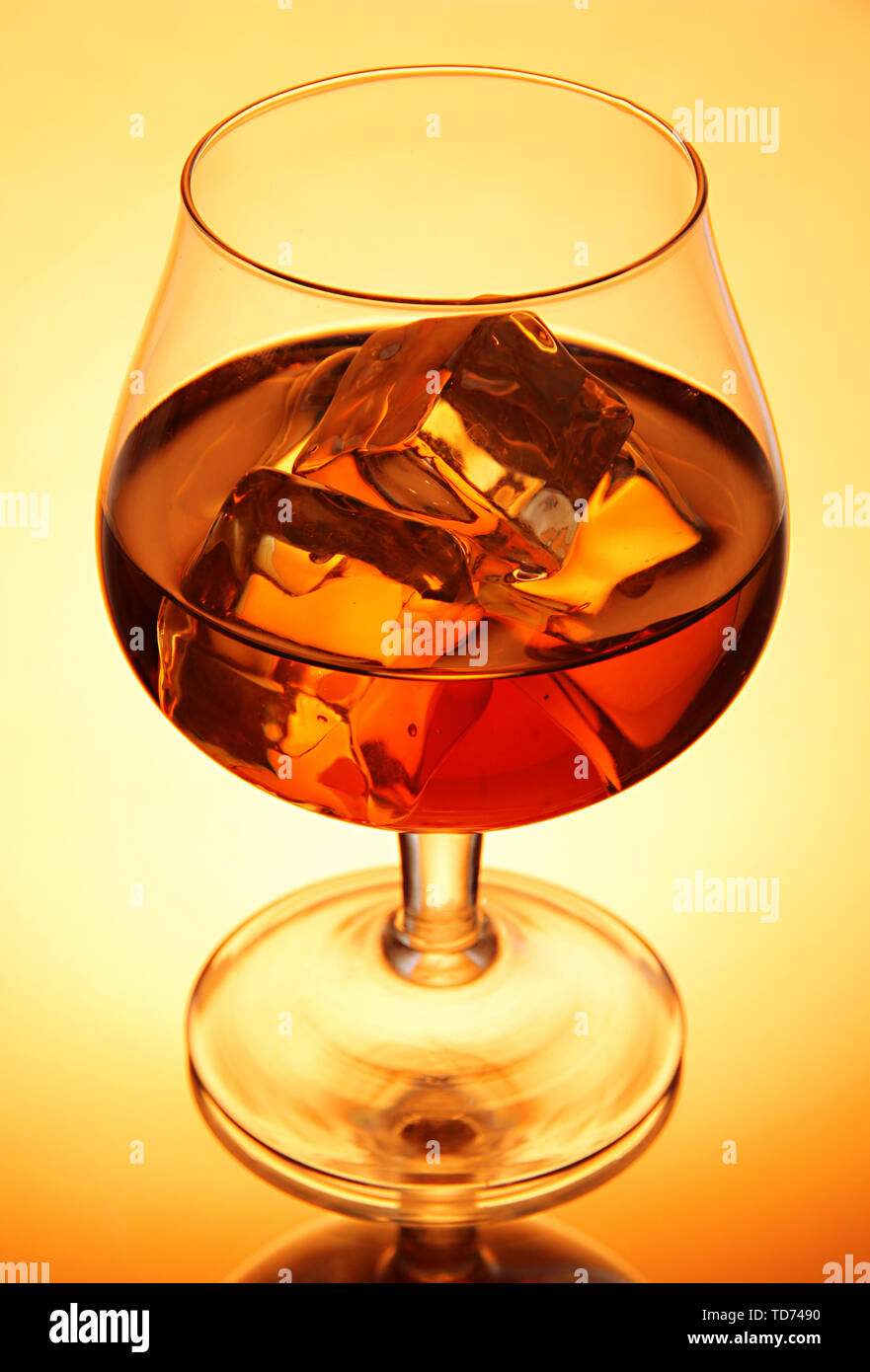 Brandy glass with ice on yellow background Stock Photo - Alamy