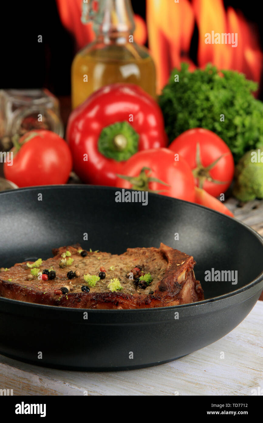 Piece of fried meat on pan on wooden table on fire background Stock ...