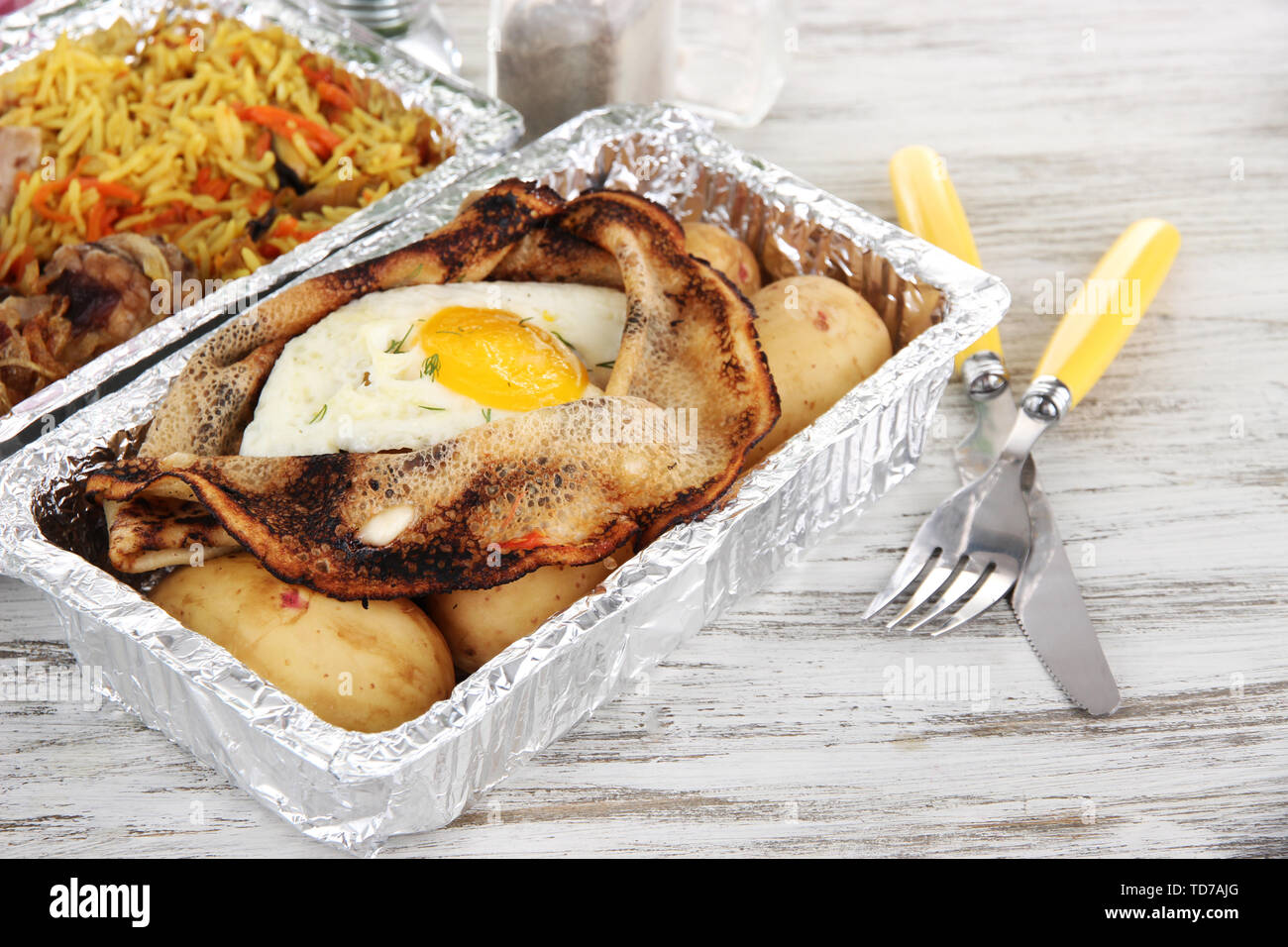 Food in boxes of foil on wooden table Stock Photo - Alamy