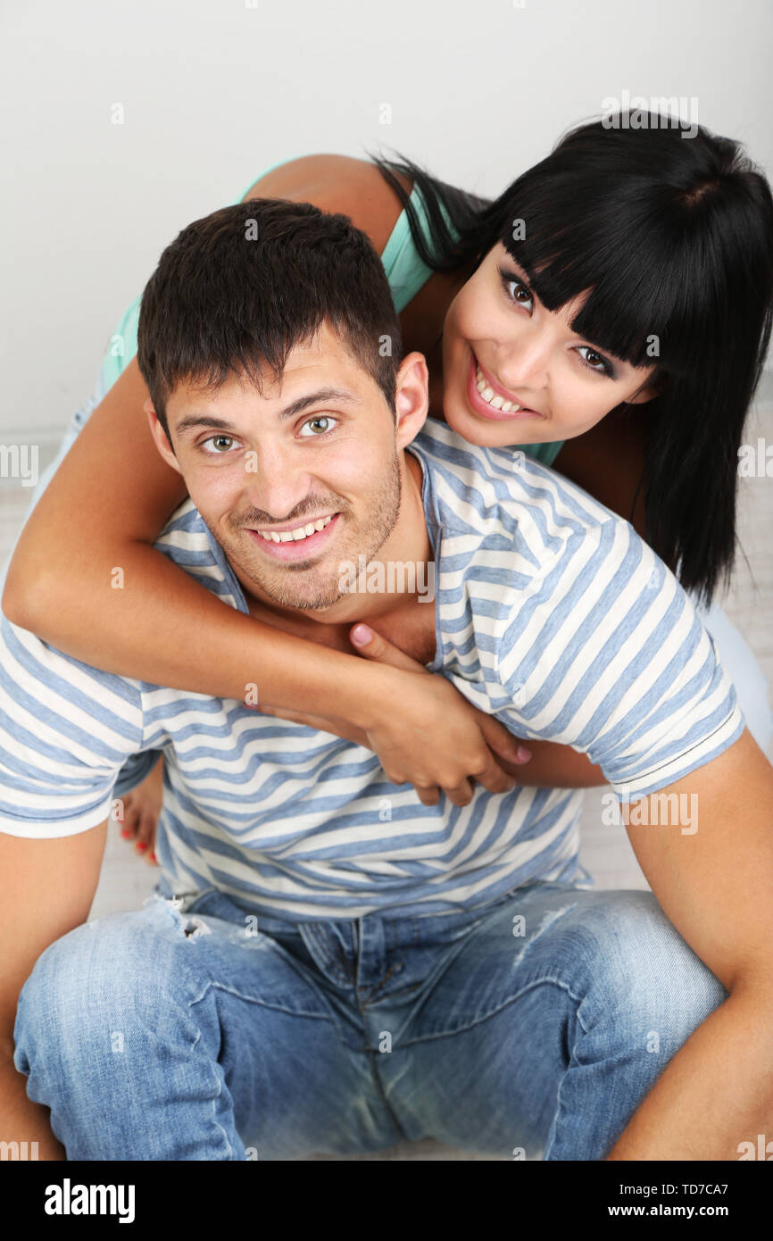 Beautiful loving couple sitting on floor in room on grey background ...