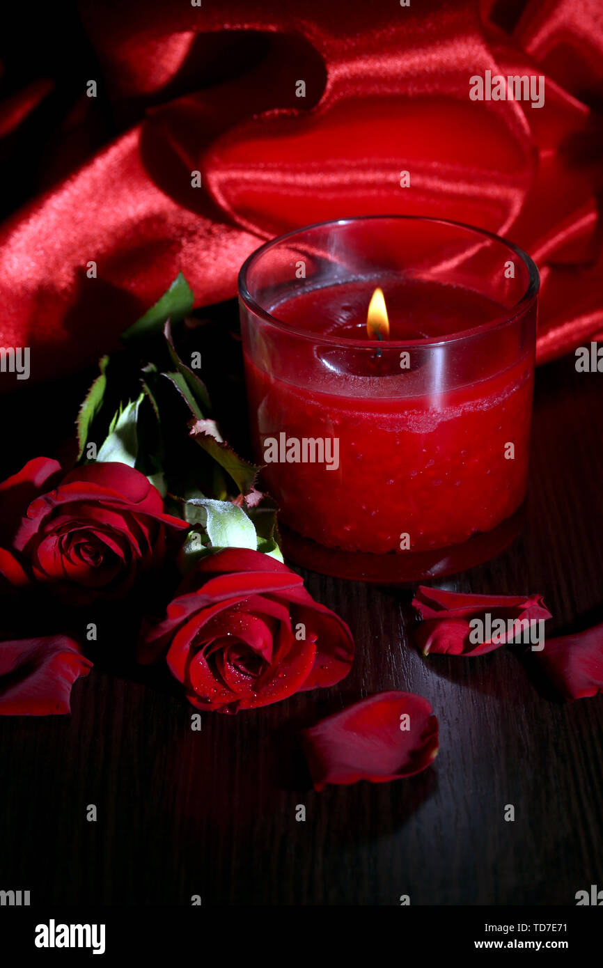 Beautiful romantic red candle with flowers and silk cloth, close up ...