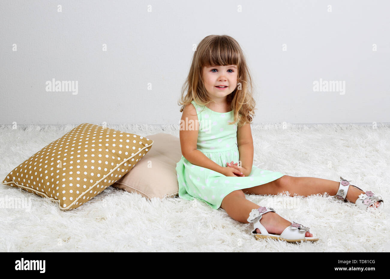 Little cute girl sitting on carpet, on gray background Stock Photo - Alamy