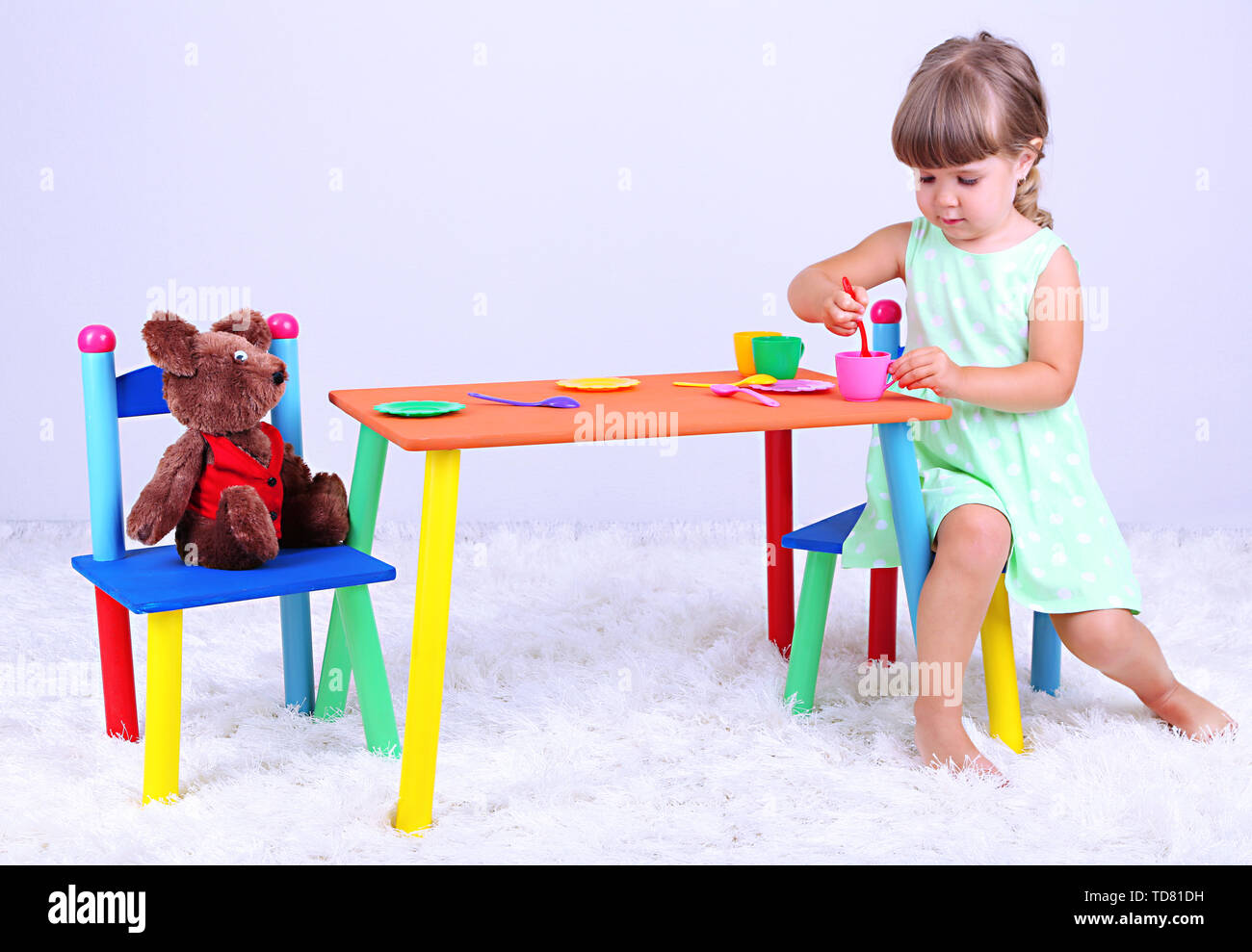 Little cute girl sitting on little chair near table, on gray background ...