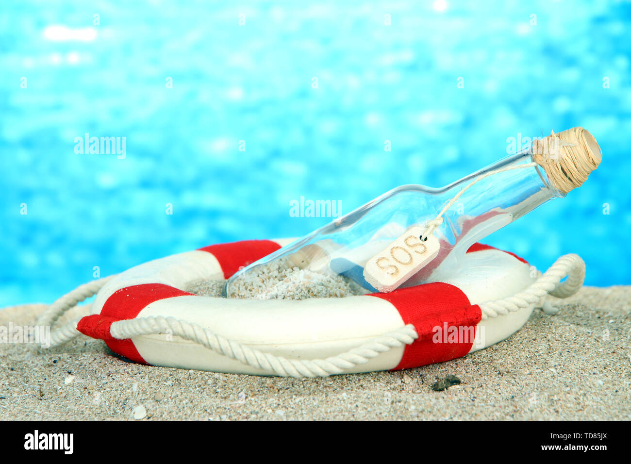Glass of bottle with note inside on sand, on bright blue background ...