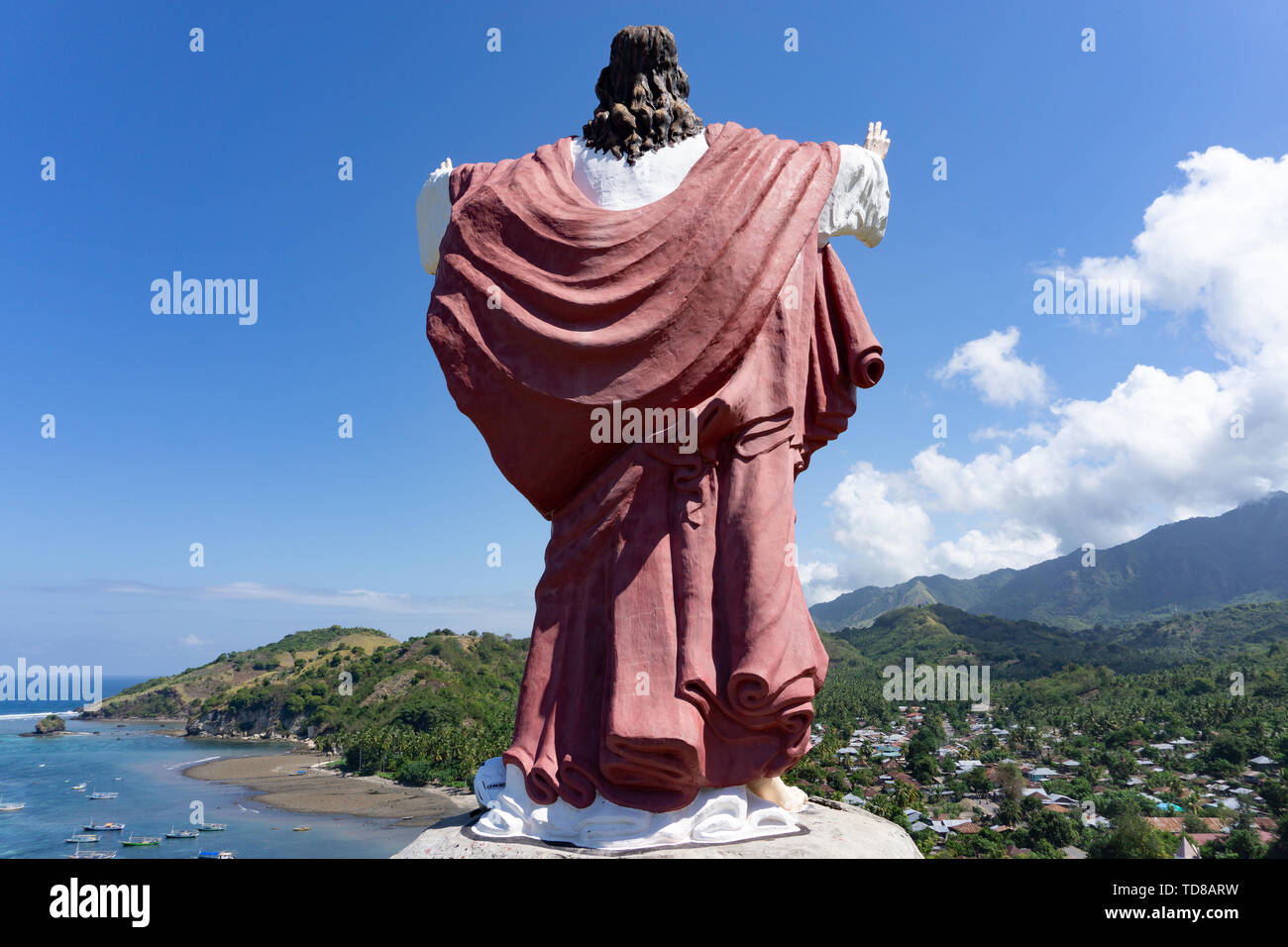 A statue of Jesus Christ laid on a hill, facing the ocean and a village ...