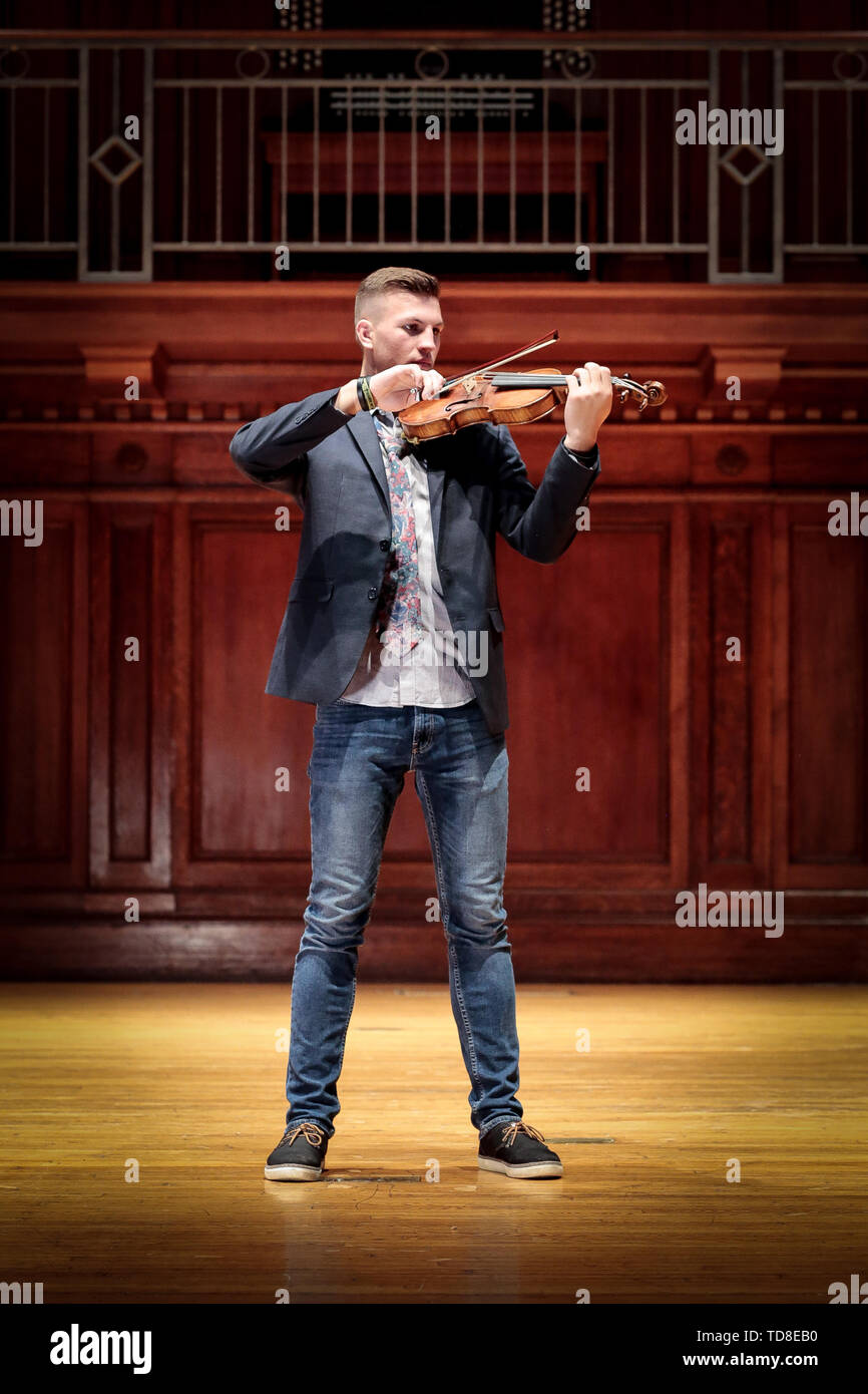 Young male violinist playing on stage with ornate wood architecture ...
