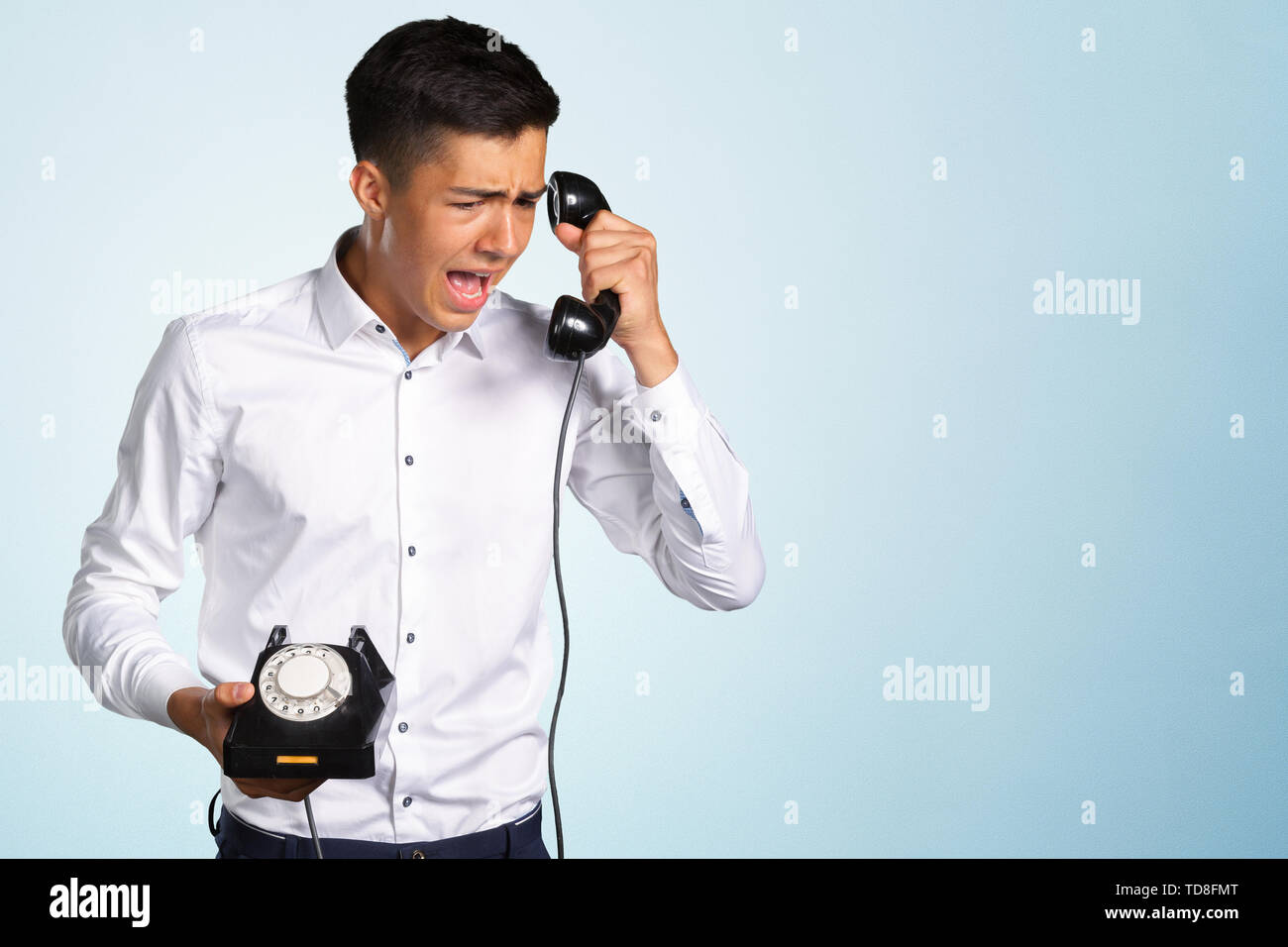 An angry and irritated young man screams into the telephone receiver ...