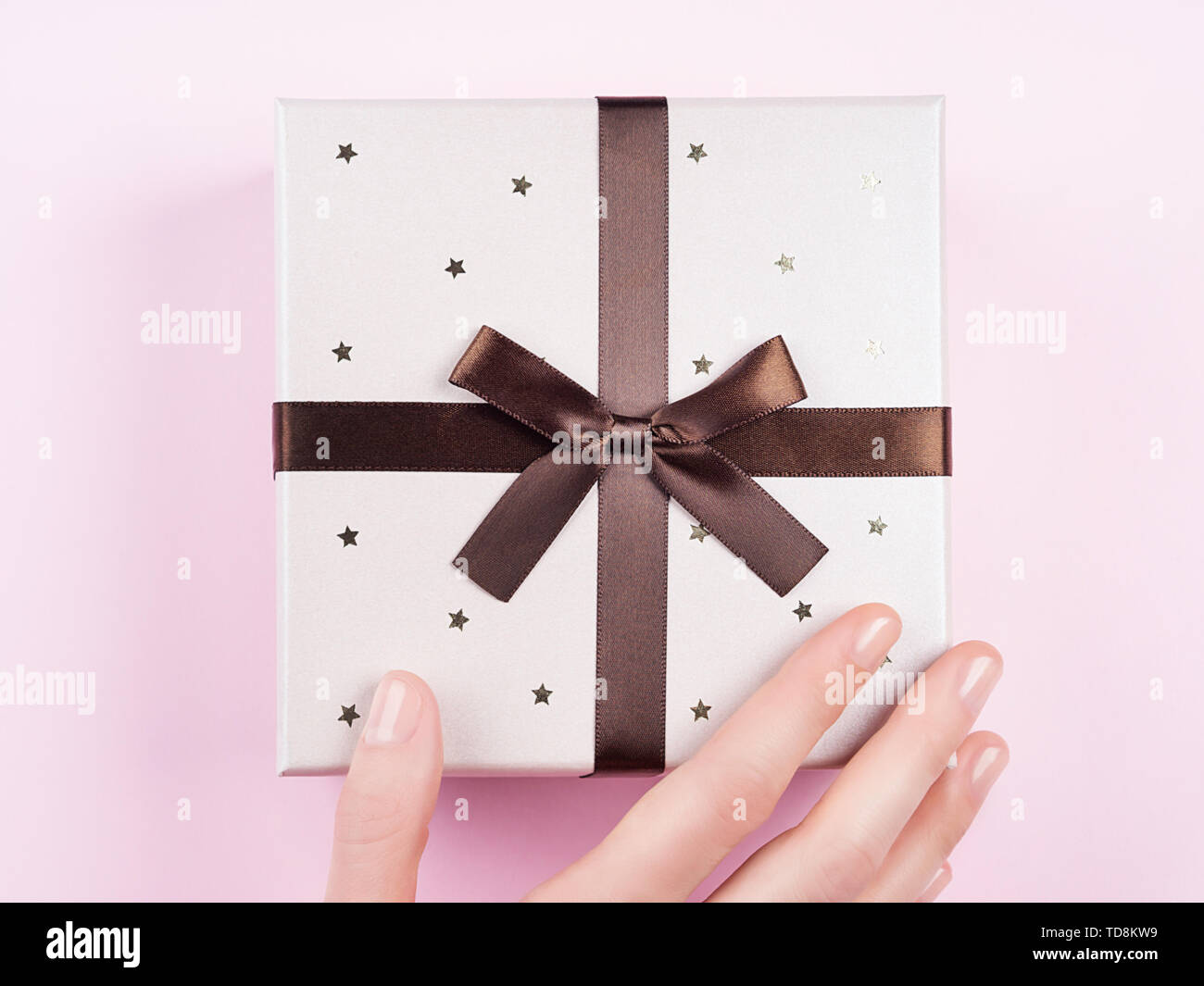 Woman's hand touching festive gift box with stars on pink background ...