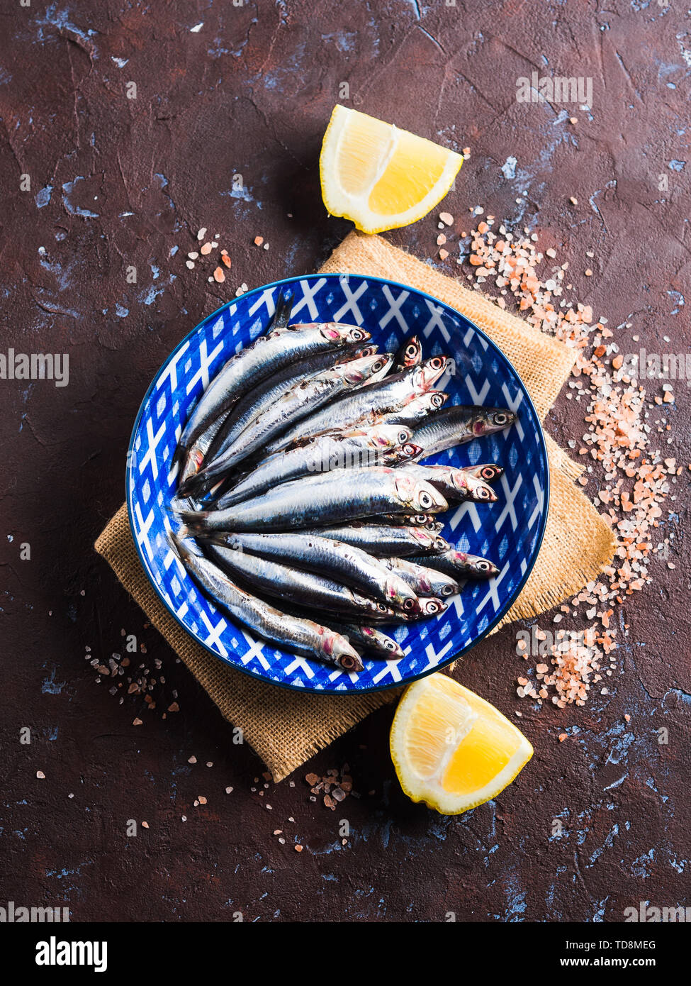 Blue fish. Fresh anchovies in a dish with pink salt and lemon on dark ...