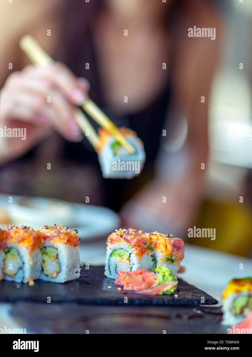 Eating sushi in the restaurant, a woman using chopsticks takes a piece ...