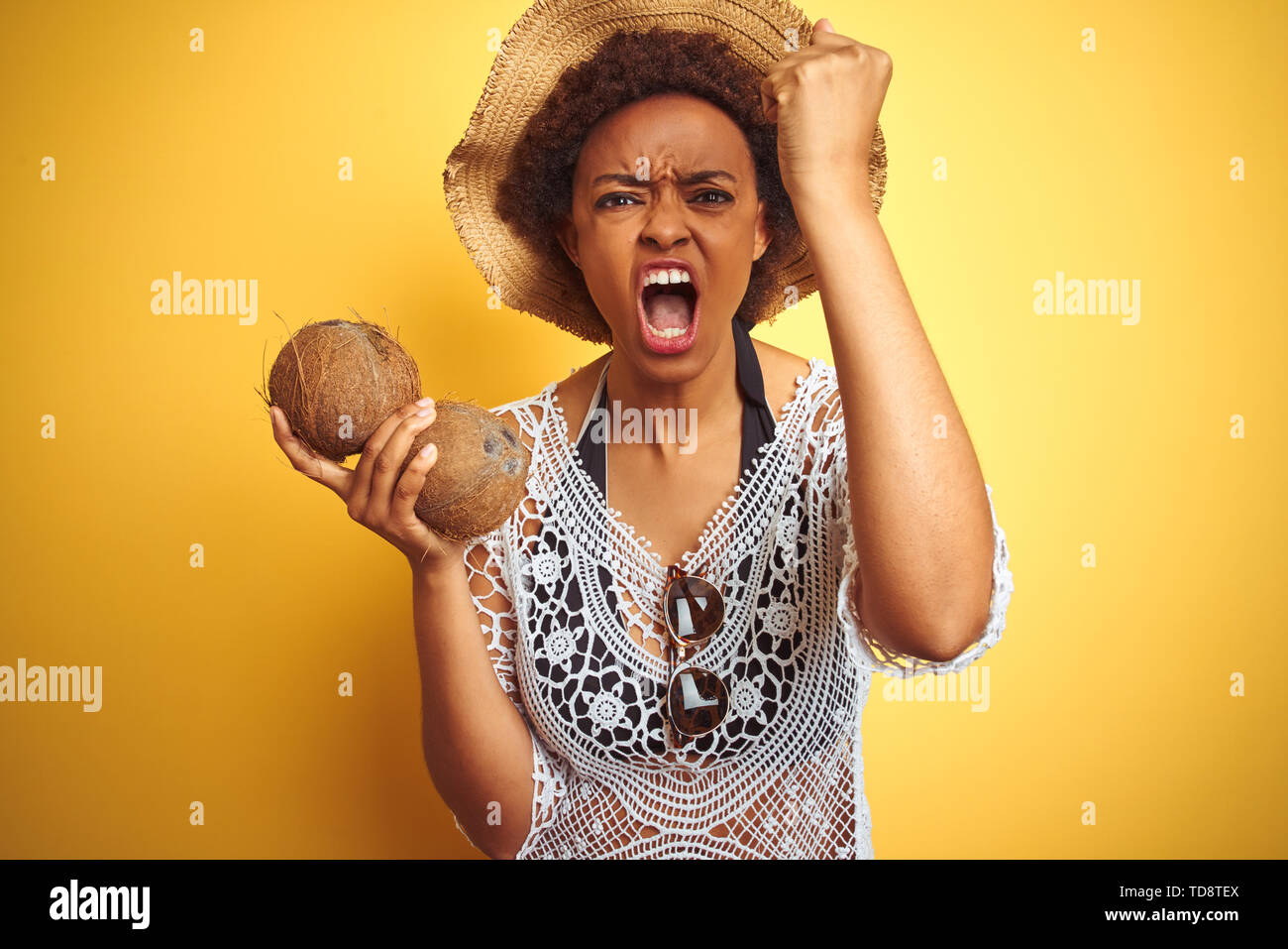 Young african american woman with afro hair holding coconut over yellow ...