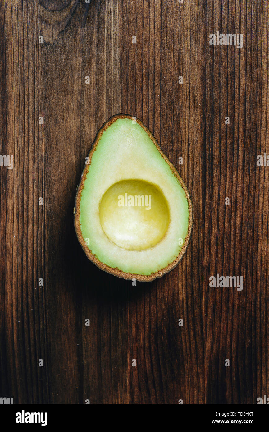 top view of half avocado without seed on wooden table, healthy vegan ...