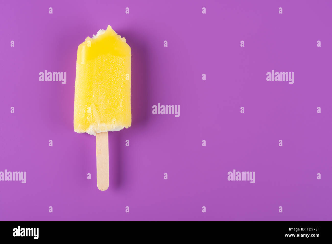yellow popsicle with couple of bites on a purple background Stock Photo ...
