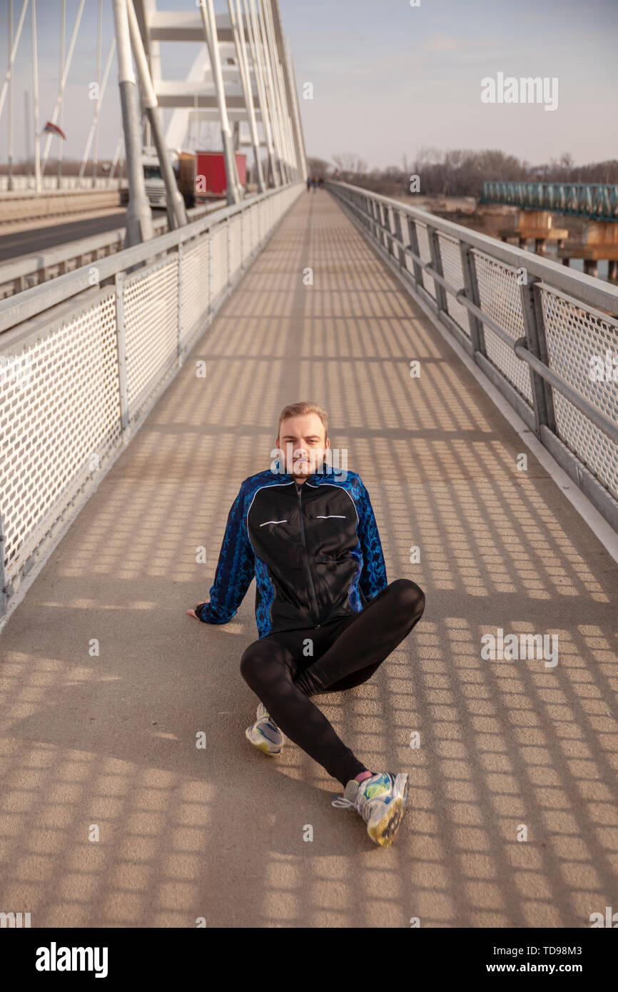 one young man, athlete and runner or jogger, sitting on a ground on a ...