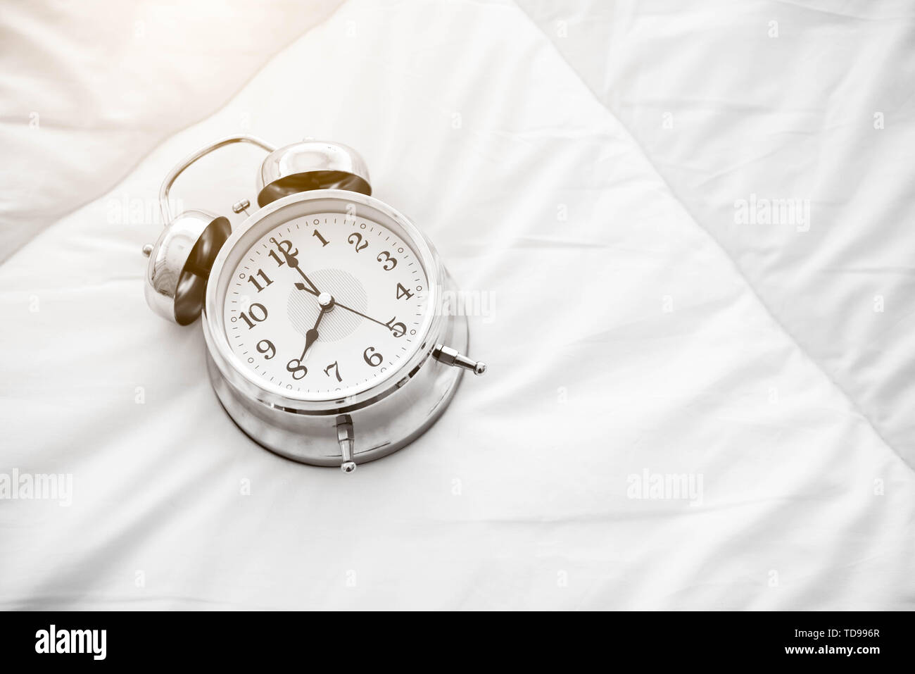 Ringing alarm clock on white bed sheet. Top view of object. 8 o clock ...