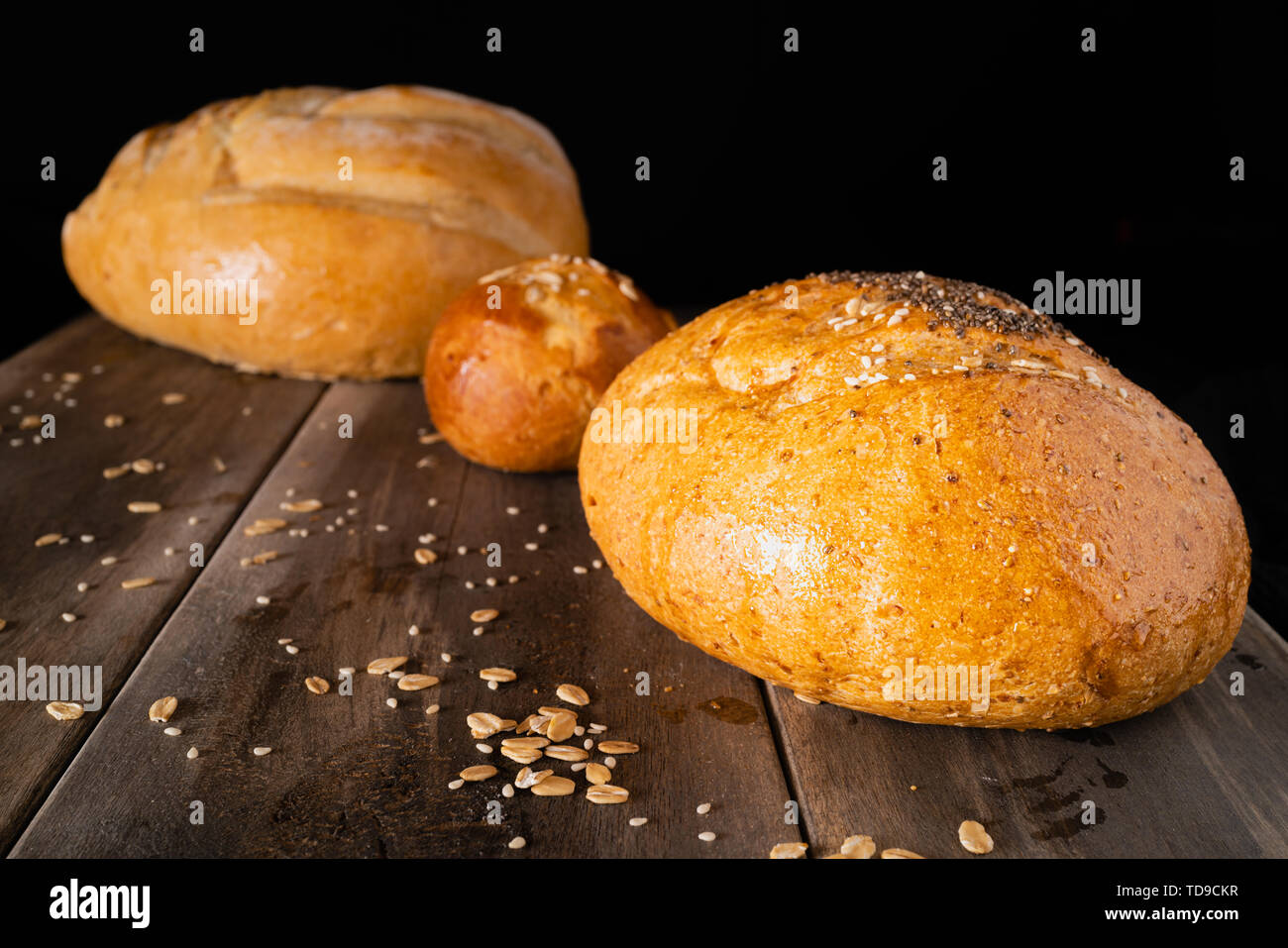 Three loaves of bread on an old wooden table with a dark background ...