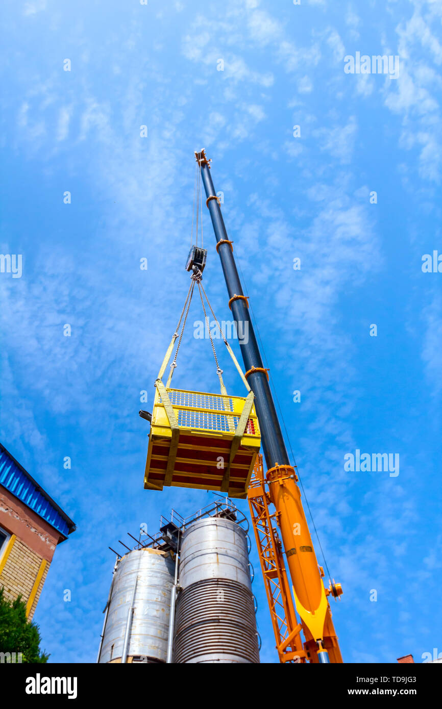 Mobile crane with hook and straps is raising work platform, basket ...