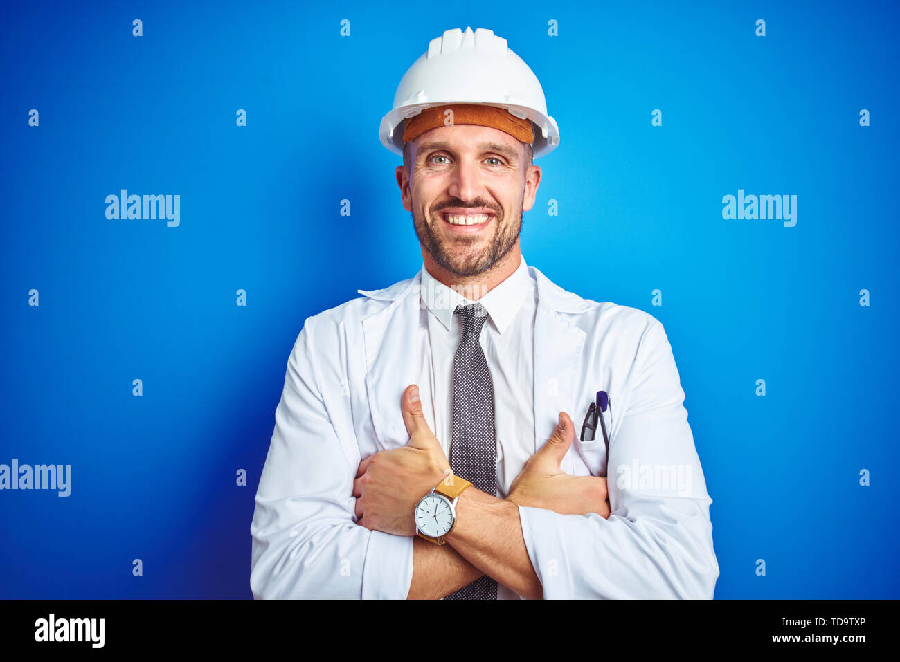 Young handsome engineer man wearing safety helmet over blue isolated ...