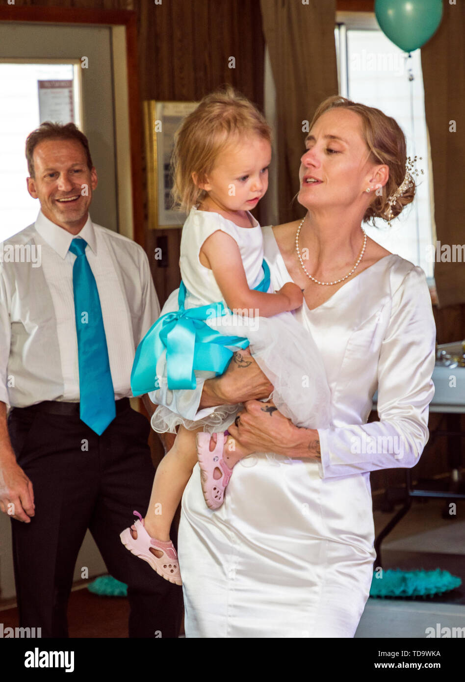 Bride holds young daughter; groom looks on; wedding reception ...