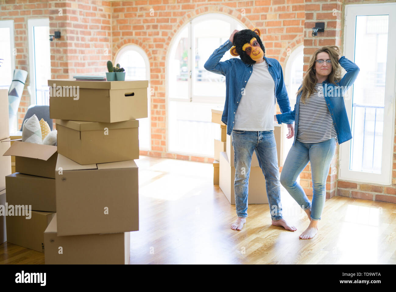 Young couple having fun wearing a monkey mask moving to a new apartment ...