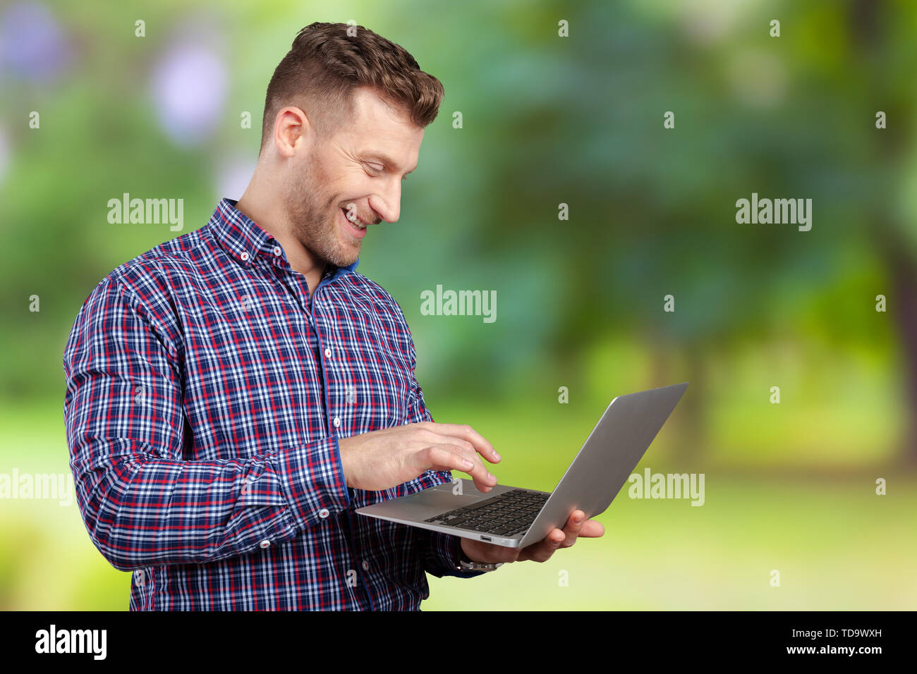 Young man standing, holding laptop computer, working Stock Photo - Alamy