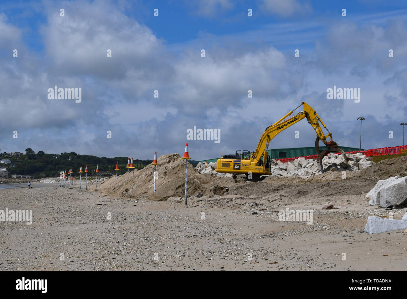 Large yellow digger moving rocks on a beach for coastal defence work in ...