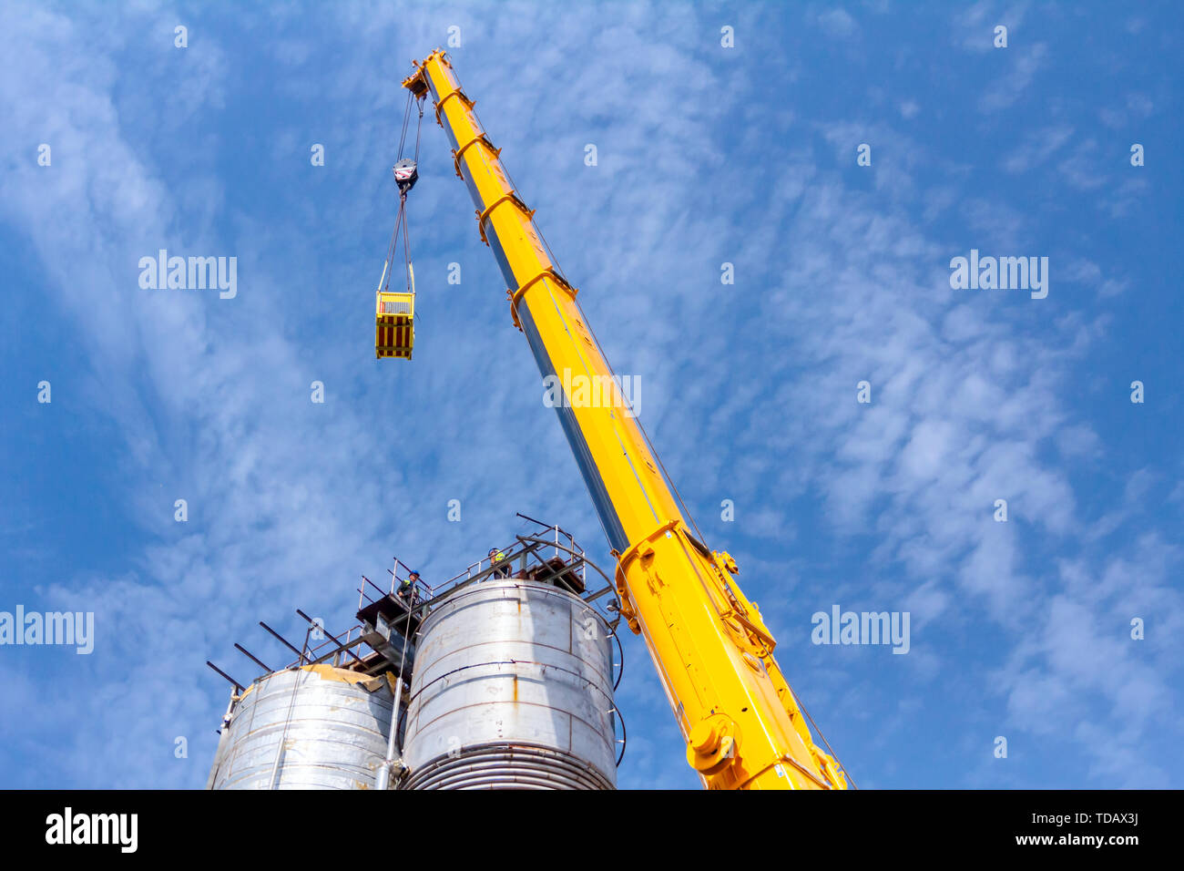 Mobile crane with hook and straps is raising work platform, basket ...