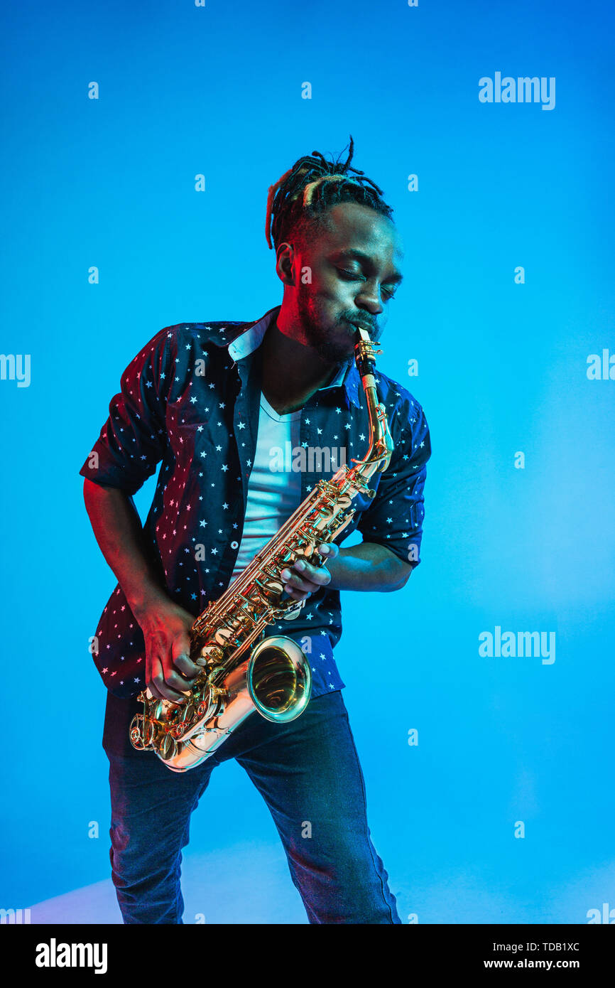Young african-american jazz musician playing the saxophone on blue ...