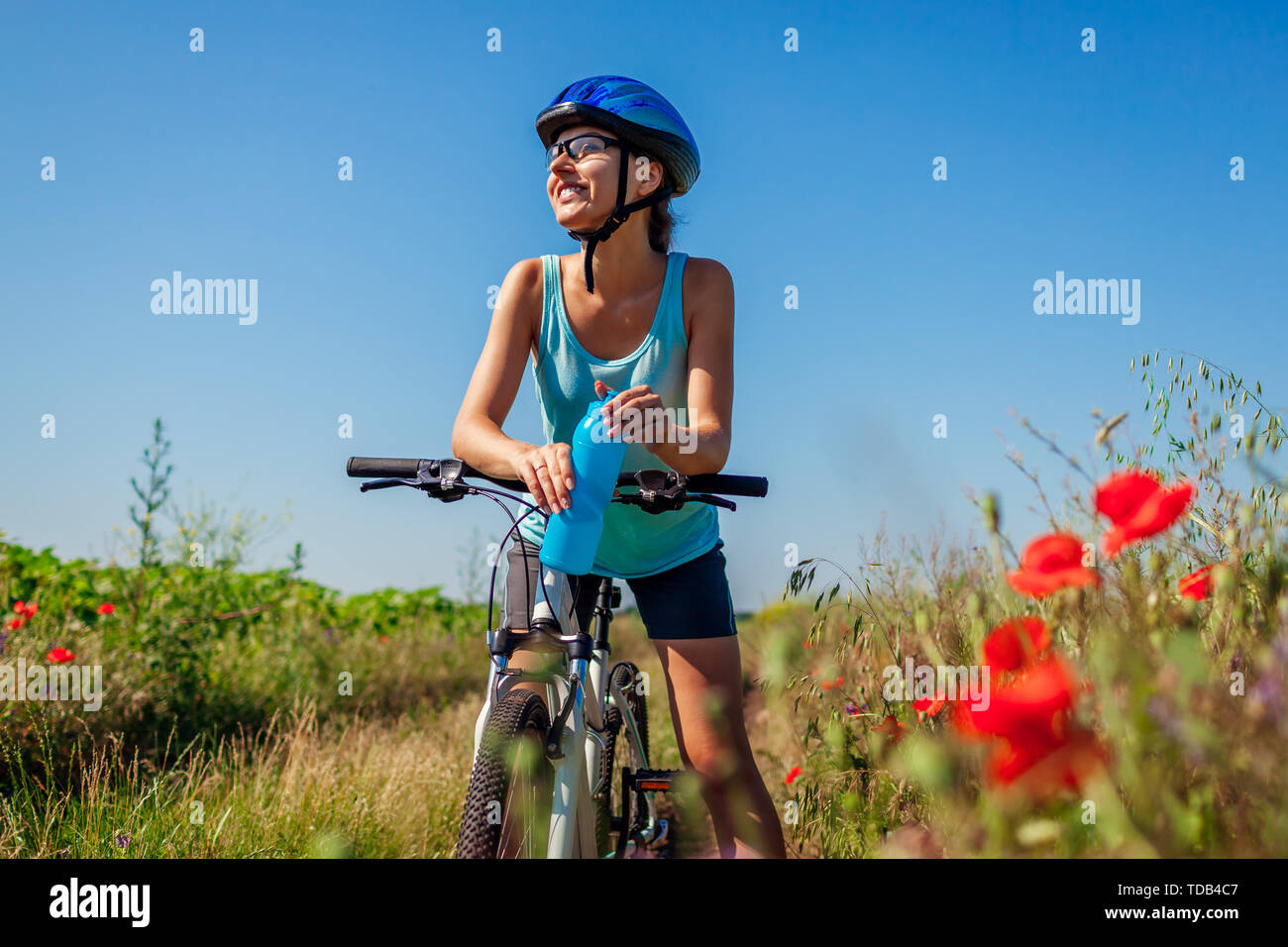 Happy young woman cyclist drinking water and having rest after riding ...